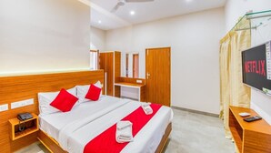 Quarto de hotel com cama, escrivaninha, televisão e ventoinha no teto.