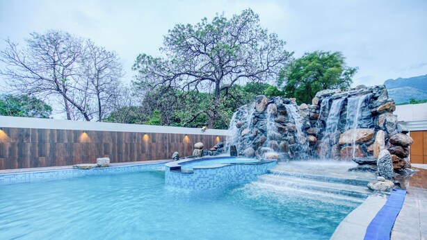 Piscina com uma cascata, rodeada por árvores e um muro de madeira.