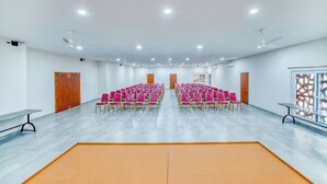 Uma sala de conferência com fileiras de cadeiras, um palco e um amplo espaço aberto.