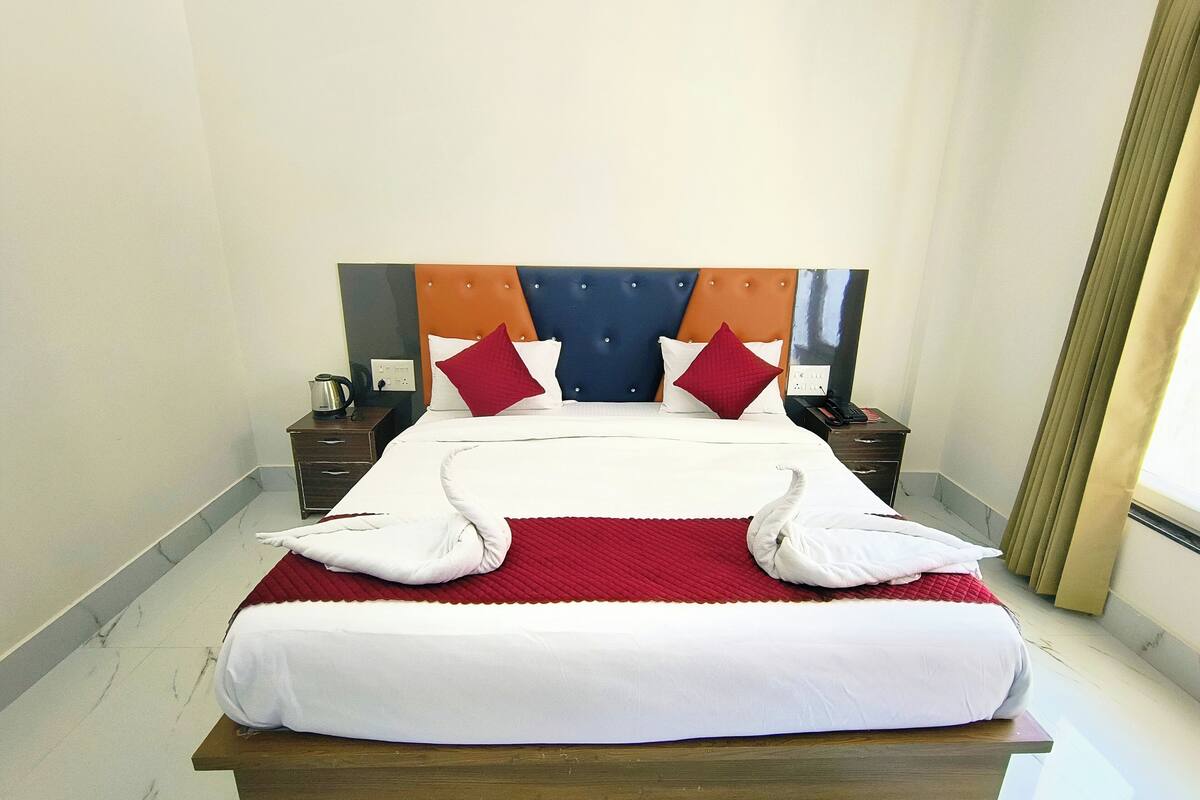 Cama bem arrumada com manta vermelha e almofadas brancas, cabeceira de madeira e mesa de cabeceira com telefone e abajur.
