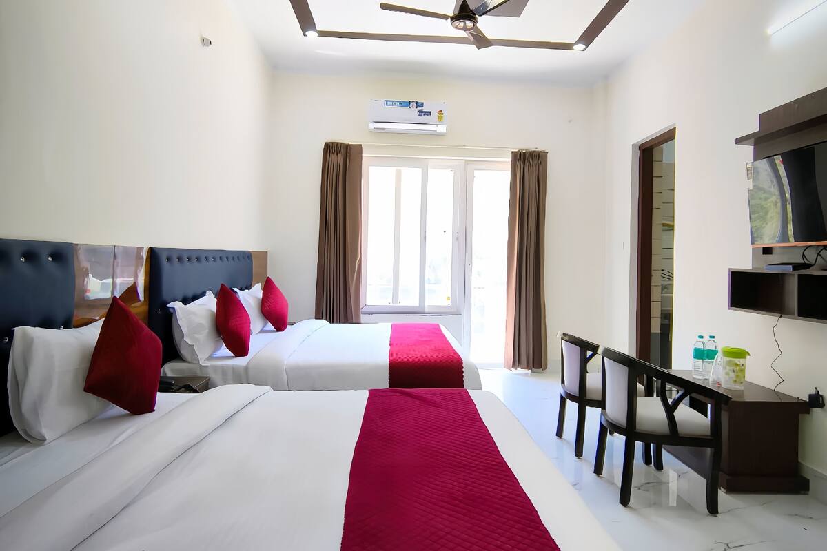 Quarto de hotel com duas camas, uma escrivaninha, uma cadeira, um ventilador de teto e um aparelho de ar condicionado.