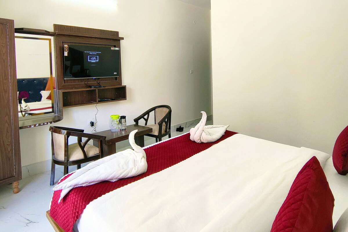 Quarto de hotel com cama, escrivaninha, cadeira, televisão e ventoinha no teto.