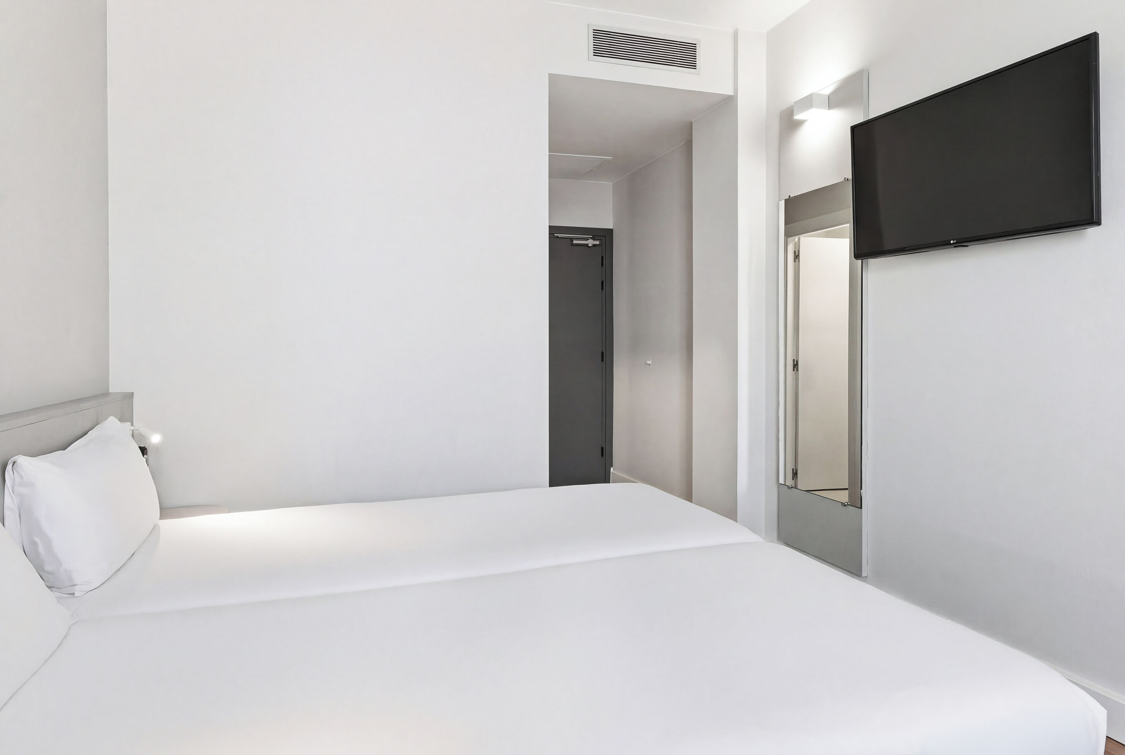 Quarto de hotel moderno com uma cama grande, televisão de tela plana na parede e porta para um banheiro.