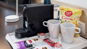 Uma bandeja com uma cafeteira, duas canecas brancas, um pacote de Frit Ravič Cajasas e diversos sachês de chá e café.