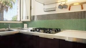 Cozinha com fogão a gás, pia de aço inoxidável e backsplash com azulejos verdes.