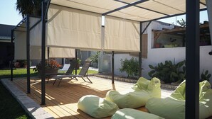 Um pátio externo com área de estar coberta, incluindo cadeiras de lounge e puffs.