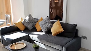Uma sala de estar moderna com um sofá cinza, almofadas estampadas, uma mesa de centro com bandeja e uma grande obra de arte emoldurada na parede.