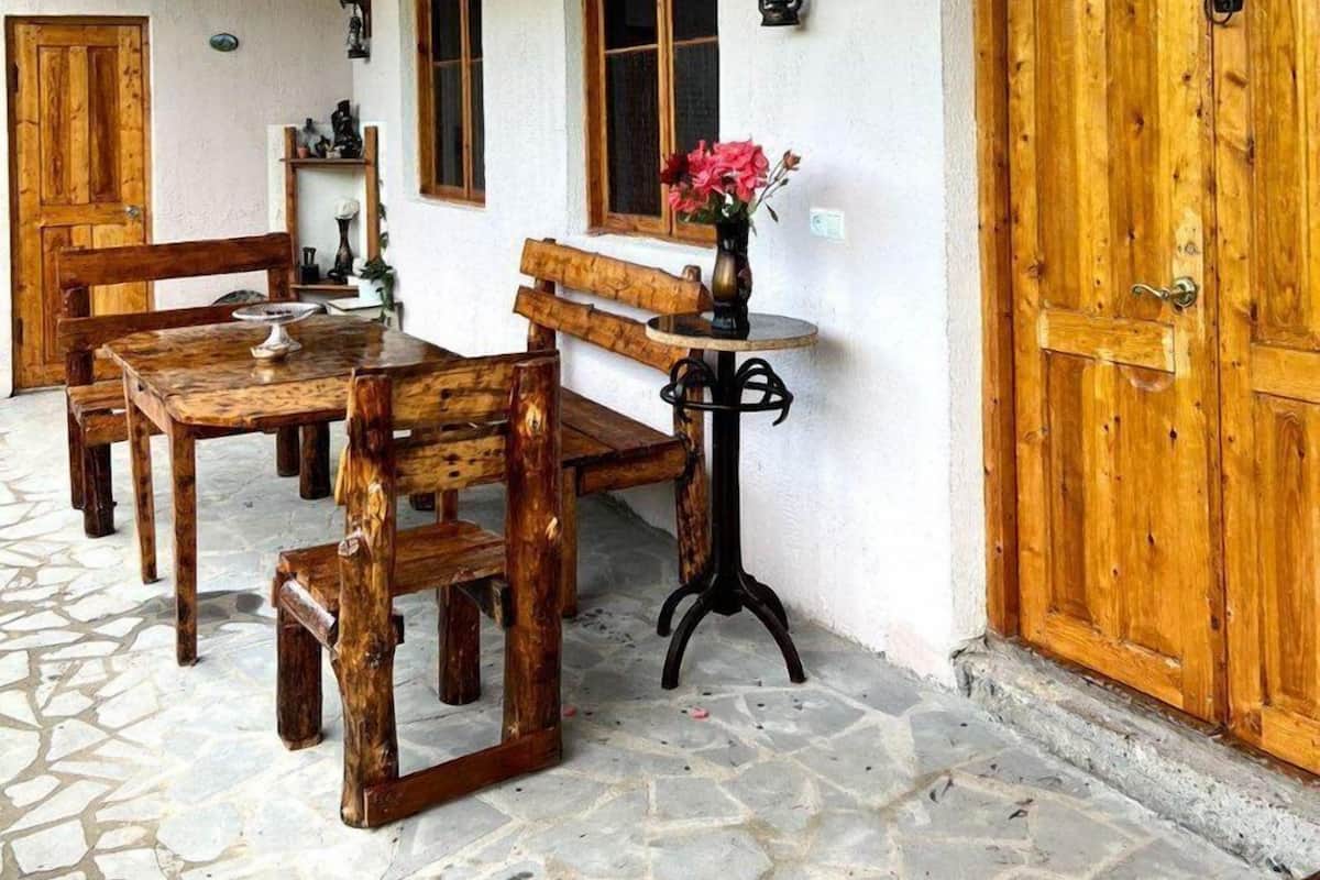 Uma área de estar rústica ao ar livre, com mobiliário de madeira, piso de ladrilho e uma grande porta de madeira.