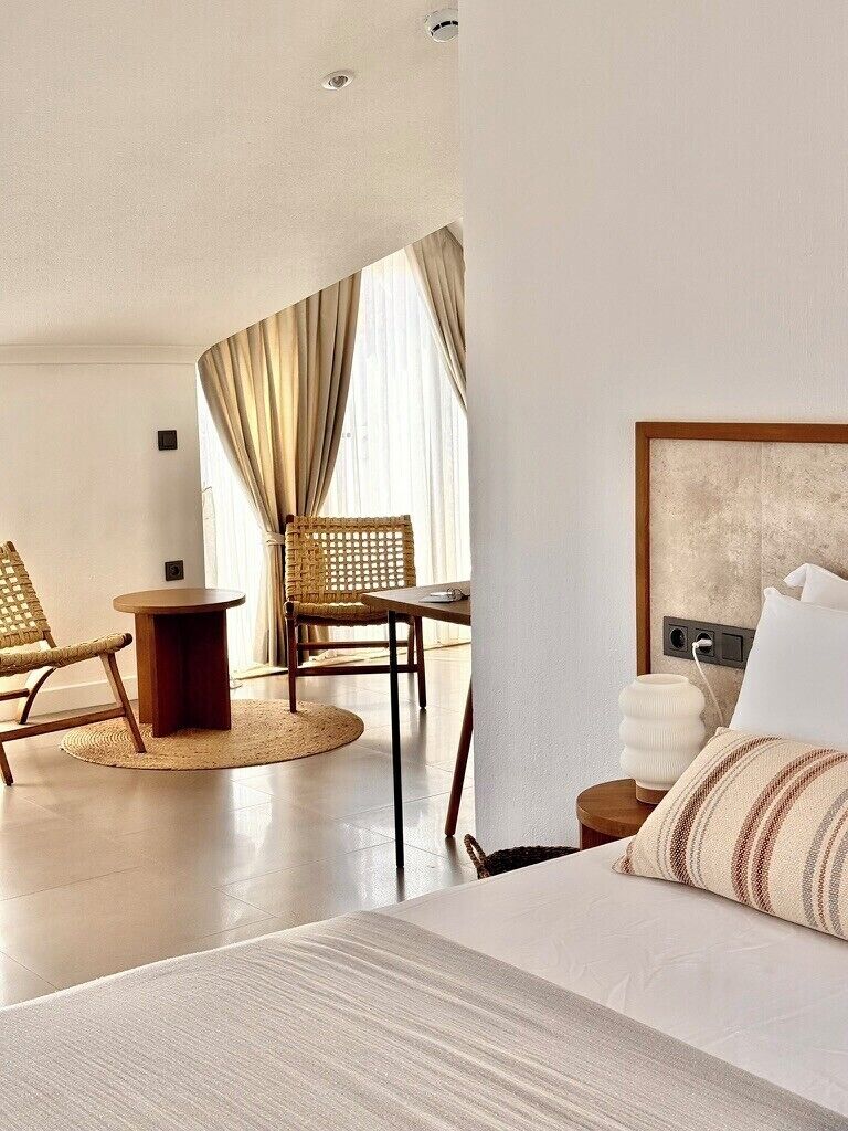 Quarto de hotel com cama, uma mesa pequena, duas cadeiras e vista para o exterior.