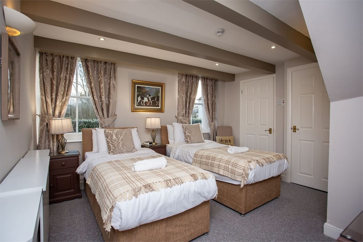 Quarto de hotel com duas camas, uma escrivaninha e um quadro na parede.