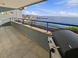 Uma varanda com churrasqueira, vista para o mar e piso de azulejos.
