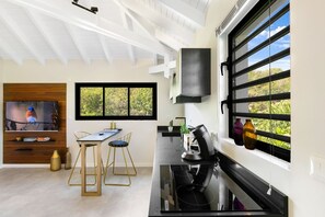 Cozinha moderna com uma janela grande, fogão embutido e área de refeições com televisão e banquetas de bar.