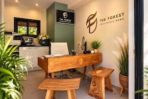 Bancada de recepção com acabamento em madeira, placa na parede para 'The Forest Suites at Anse Marcel' e uma janela com vista para o verde.
