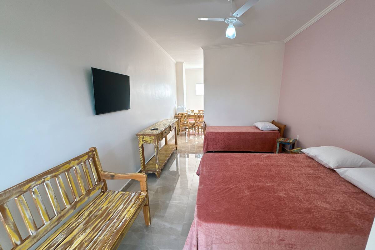 Quarto com duas camas, um banco de madeira, uma mesa e um ventilador de teto.