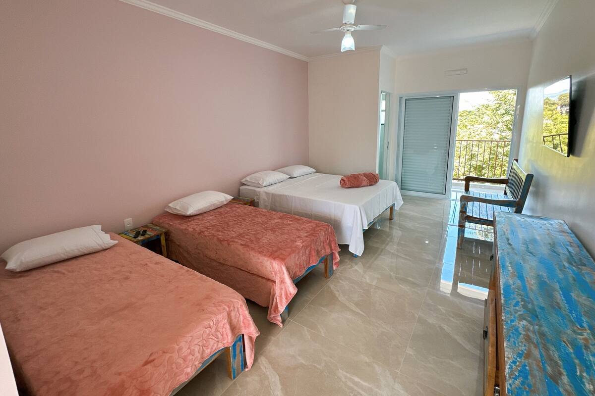 Quarto de hotel com duas camas, ventoinha no teto, televisão e varanda com vista.