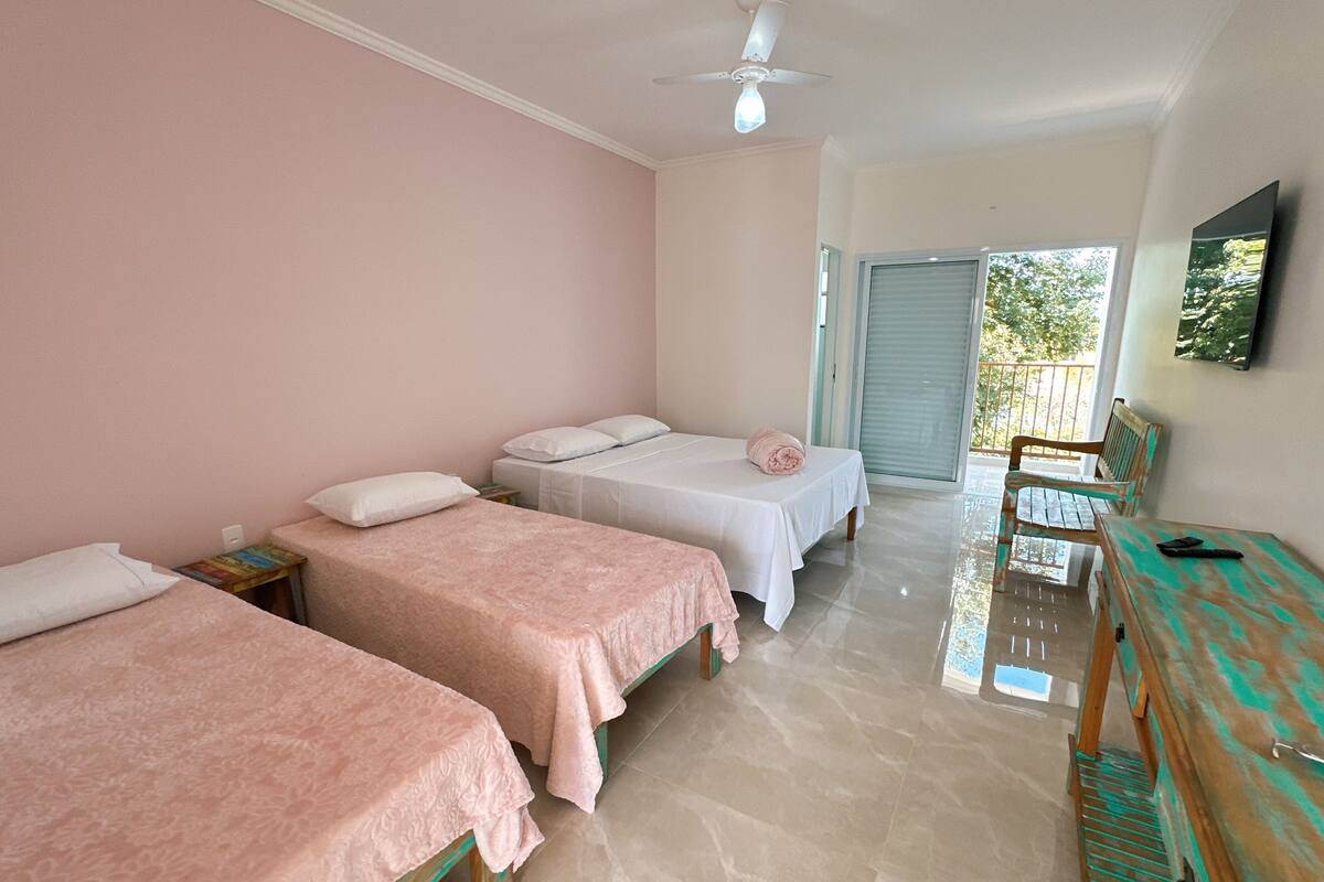Quarto de hotel com duas camas, televisão, varanda e ventoinha no teto.
