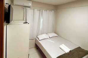 Quarto pequeno com cama de solteiro, uma cama branca, TV branca em um suporte e ar condicionado branco acima da cama.