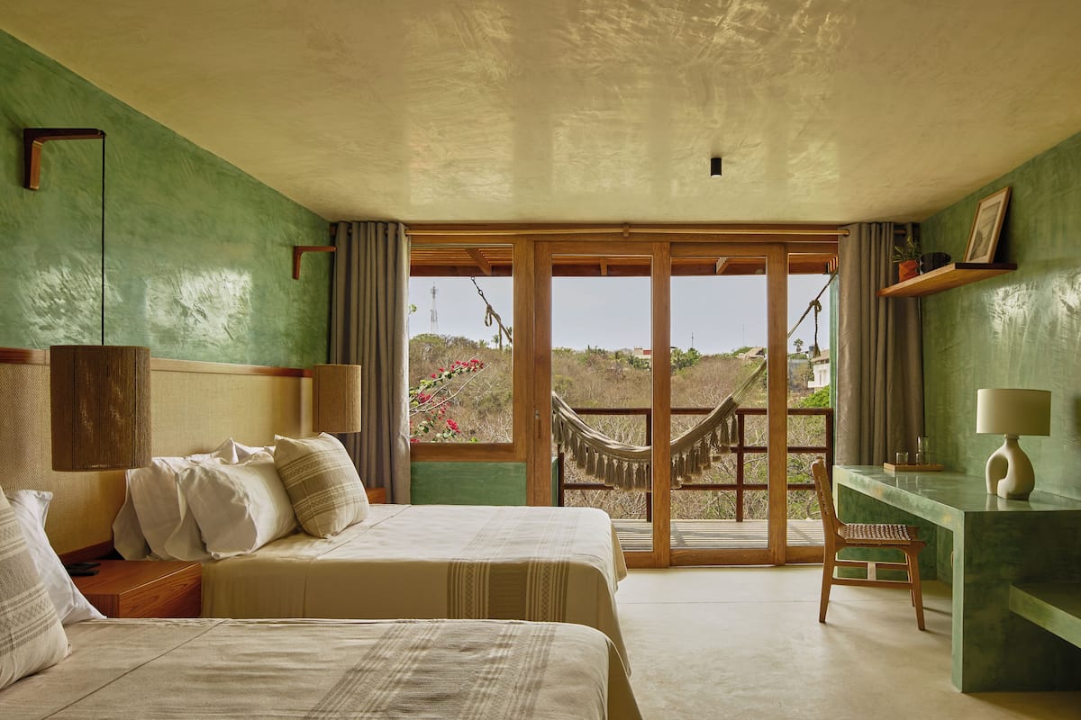 Quarto com duas camas, uma mesa de escritório e vista para a paisagem através de uma grande porta deslizante.