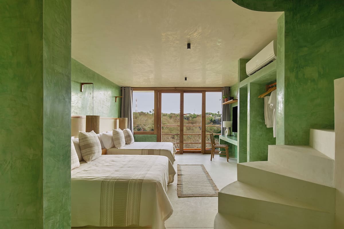 Quarto com duas camas, um lance de escadas e vista para o exterior.