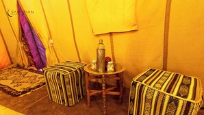 Uma área com tendas, almofadas estampadas, uma pequena mesa redonda com uma garrafa e um tapete.