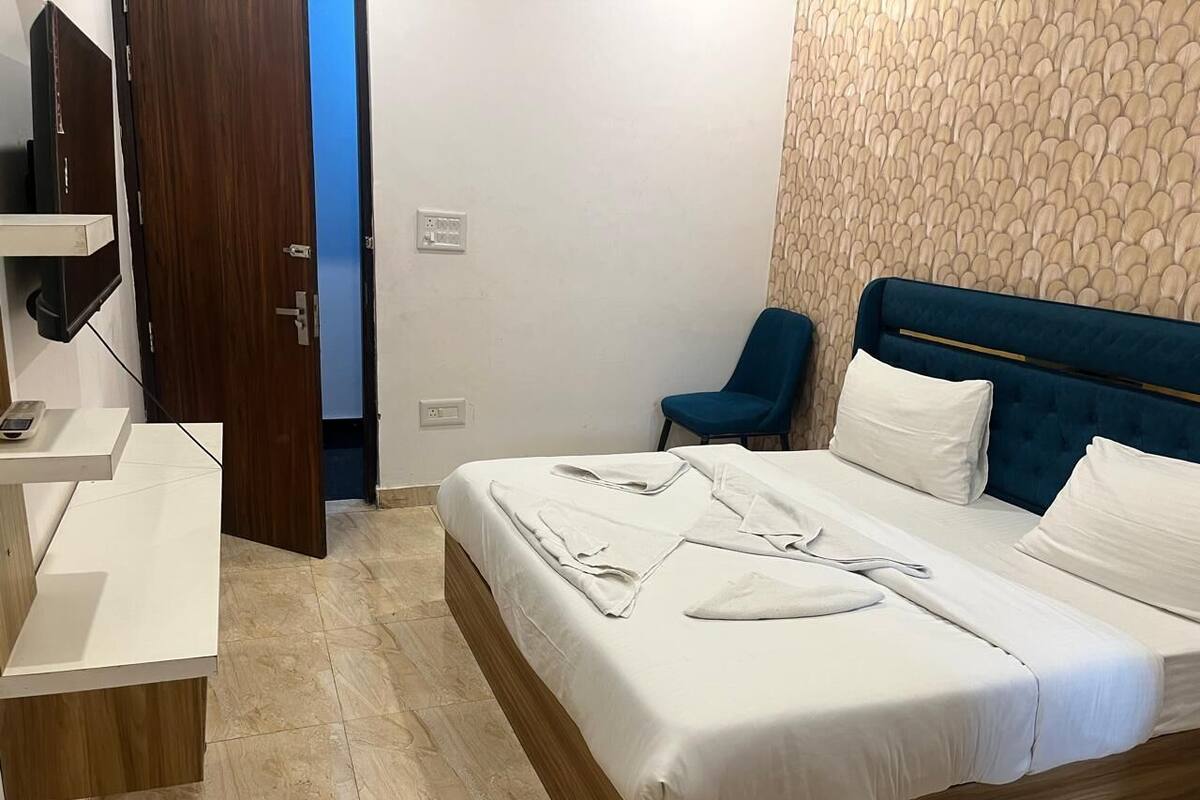 Quarto de hotel com cama, escrivaninha, cadeira e televisão.
