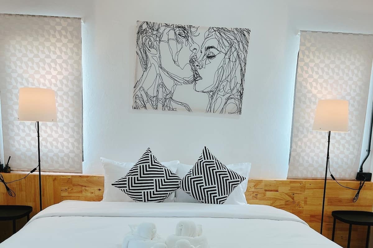 Quarto de hotel com uma cama grande, duas almofadas estampadas, uma obra de arte na parede e duas luminárias de cabeceira.