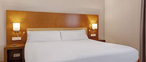 Quarto de hotel com uma cama grande, luminárias de cabeceira, mesa de cabeceira e cabeceira de madeira.