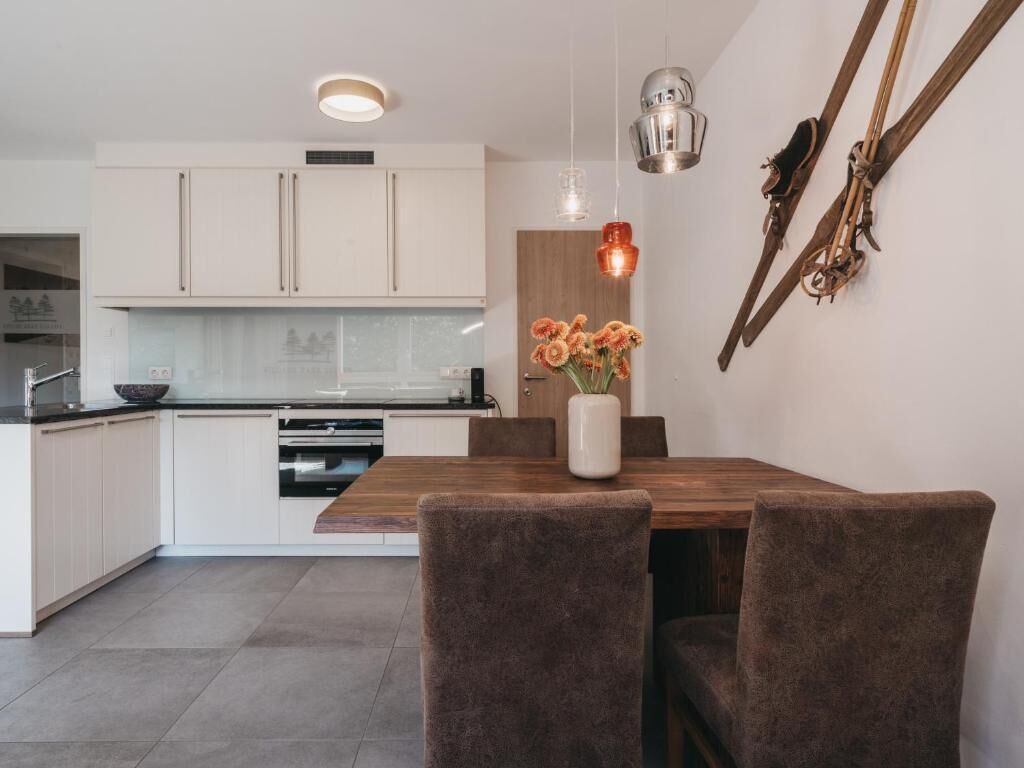 Cozinha moderna com armários brancos, uma mesa de jantar de madeira e duas cadeiras. Há um vaso com flores na mesa e um par de esquis pendurados na parede.