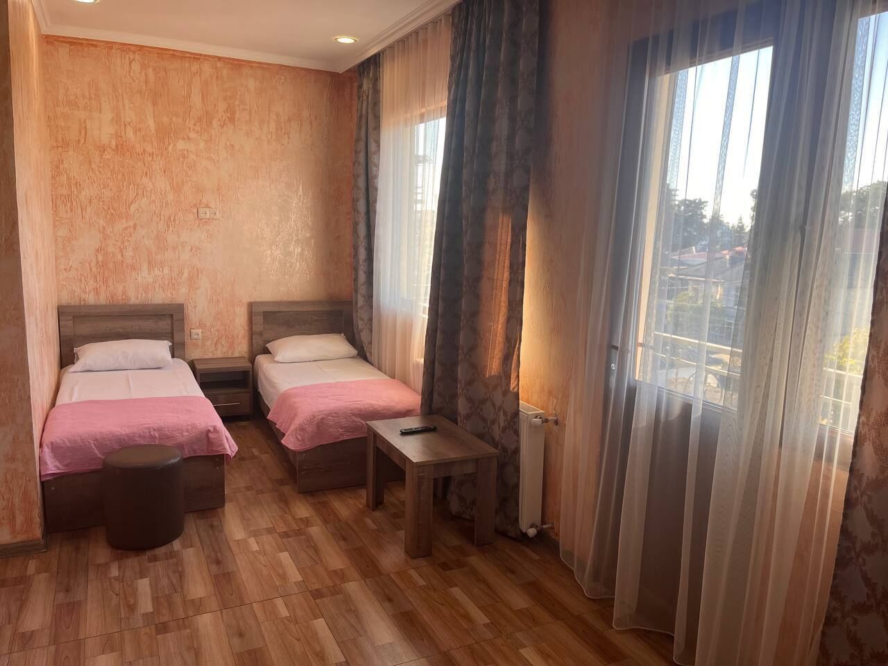 Quarto de hotel com duas camas, uma mesa pequena e janela com cortinas.