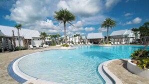 Piscina com espreguiçadeiras e palmeiras, cercada por edifícios com telhados brancos.