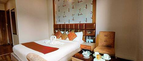 Quarto de hotel com uma cama grande, cabeceira de madeira, mesa de cabeceira com abajur e uma cadeira.