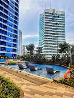 Área de piscina com espreguiçadeiras, uma boia salva-vidas e edifícios altos ao fundo.