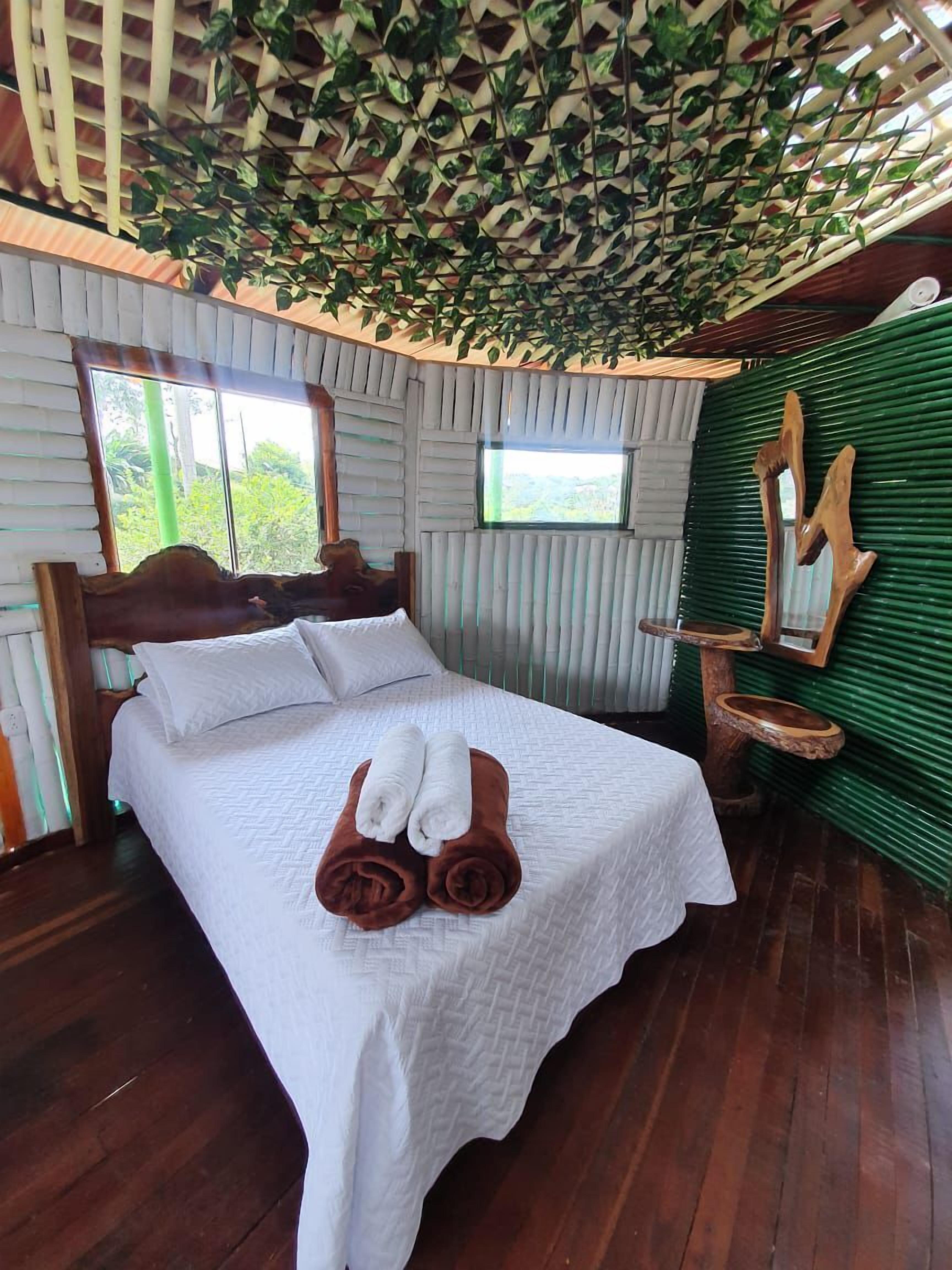 Quarto com cama, cabeceira de madeira, janela e parede verde com escultura de madeira.