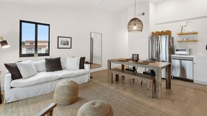 Uma sala de estar moderna com um sofá branco, uma mesa de jantar de madeira e uma cozinha com frigorífico, micro-ondas e torradeira.