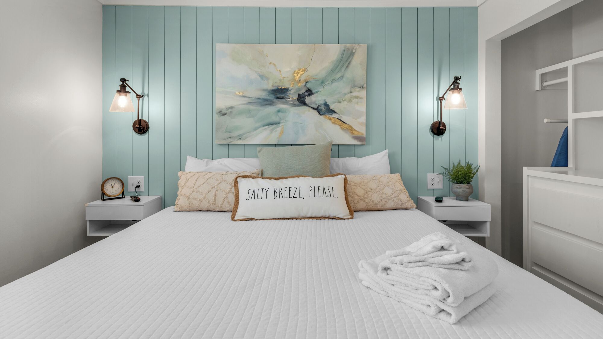 Cama bem arrumada com um travesseiro que diz 'SALTY BREEZE, PLEASE'.