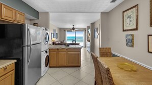 Cozinha equipada com frigorífico, máquina de lavar roupa e zona de refeições com vista para o mar.