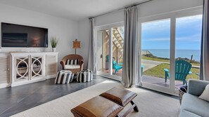 Sala de estar com televisão, cadeira de vime, sofá e vista para o mar.