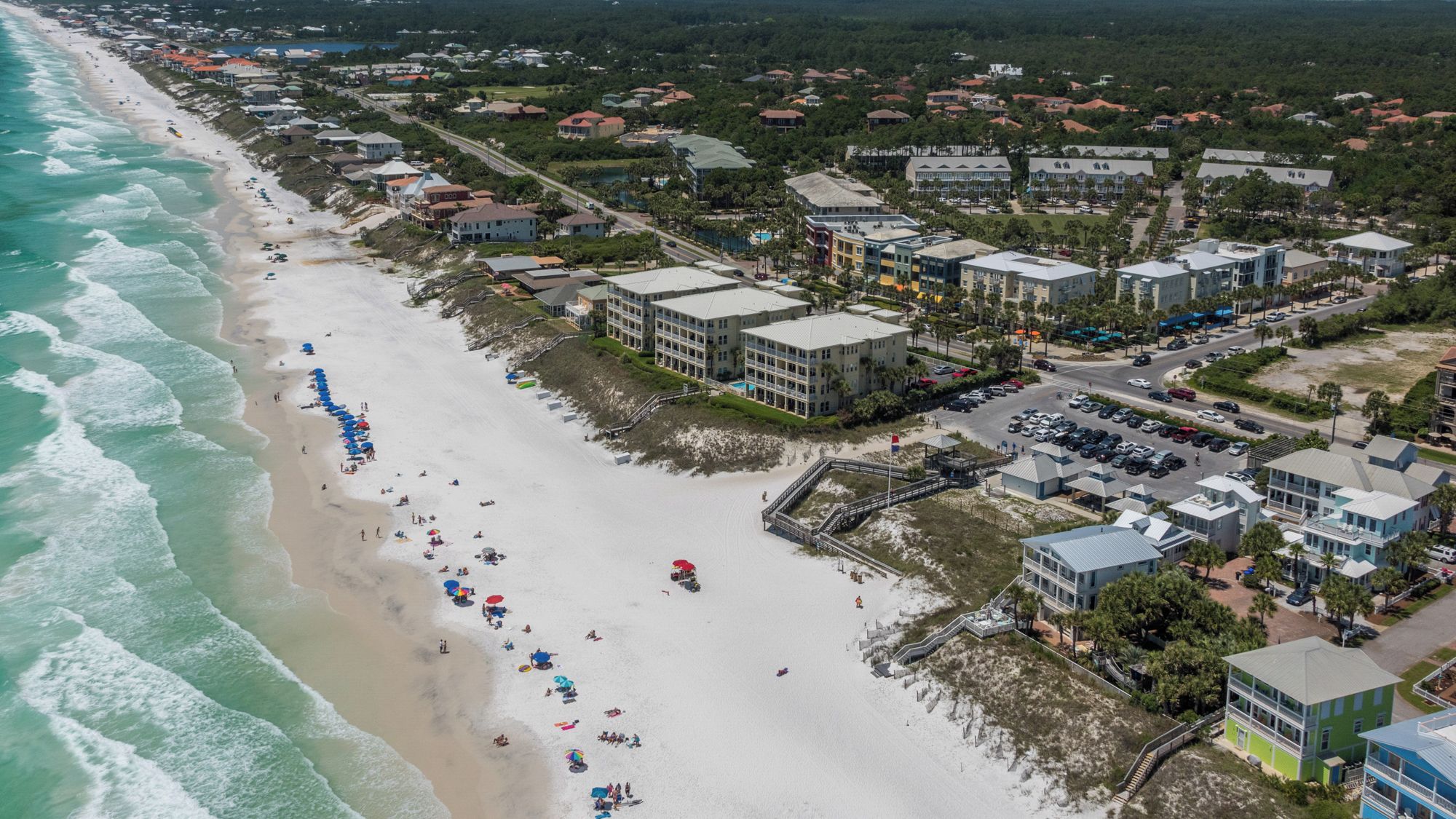 Vista aérea de um resort à beira-mar, com uma extensa faixa de areia, vários edifícios de hotel e um estacionamento.