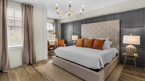 Quarto com uma cama grande, duas luminárias de cabeceira, um lustre e vista para o exterior pela janela.