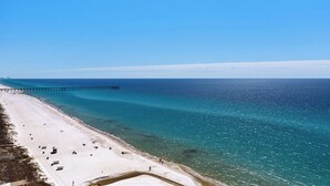 Uma praia com um píer que se estende para o oceano, areal arenoso e águas azul-claras.