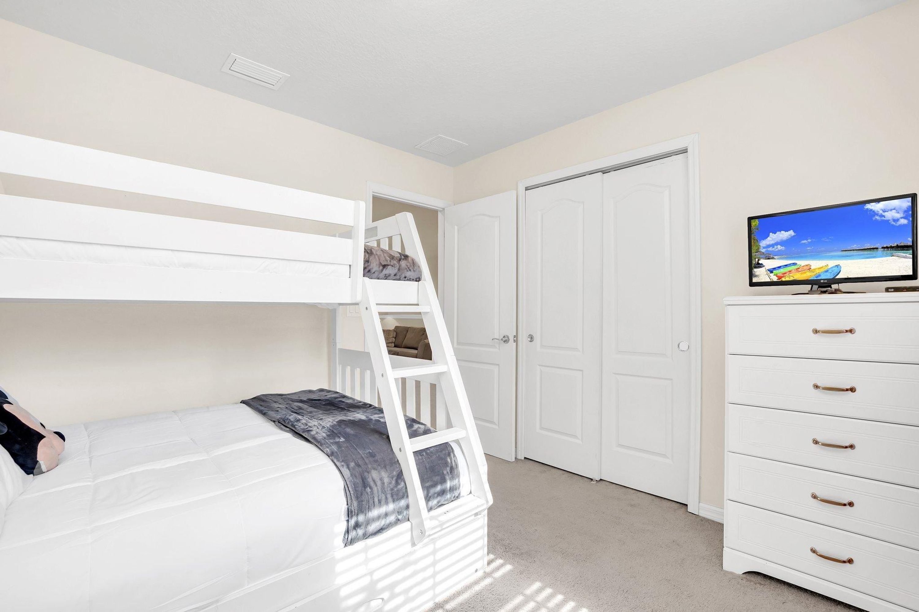 Quarto com cama de solteiro e beliche, cômoda, televisão e armário.