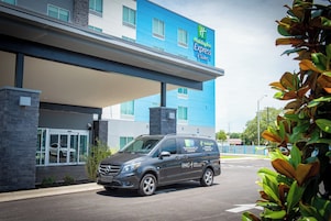 Edifício do Holiday Inn Express & Suites com design moderno, fachada azul e área de estacionamento com uma van Mercedes-Benz.
