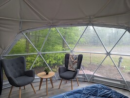 Quarto com tenda, duas cadeiras, uma mesa pequena e uma cama.