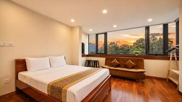 Quarto com cama, sofá, janela com vista e piso de madeira.