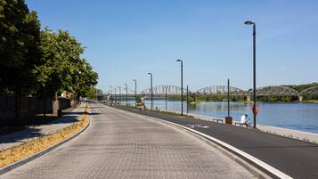 Uma passarela pavimentada ao longo de um rio, com uma ponte ao fundo.