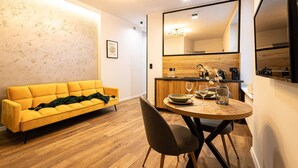 Uma sala de estar moderna com um sofá amarelo, uma mesa de jantar com cadeiras e uma área de cozinha com bancada de madeira e um espelho.