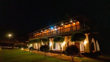 Um edifício de dois andares com varanda, iluminado por uma luz quente.