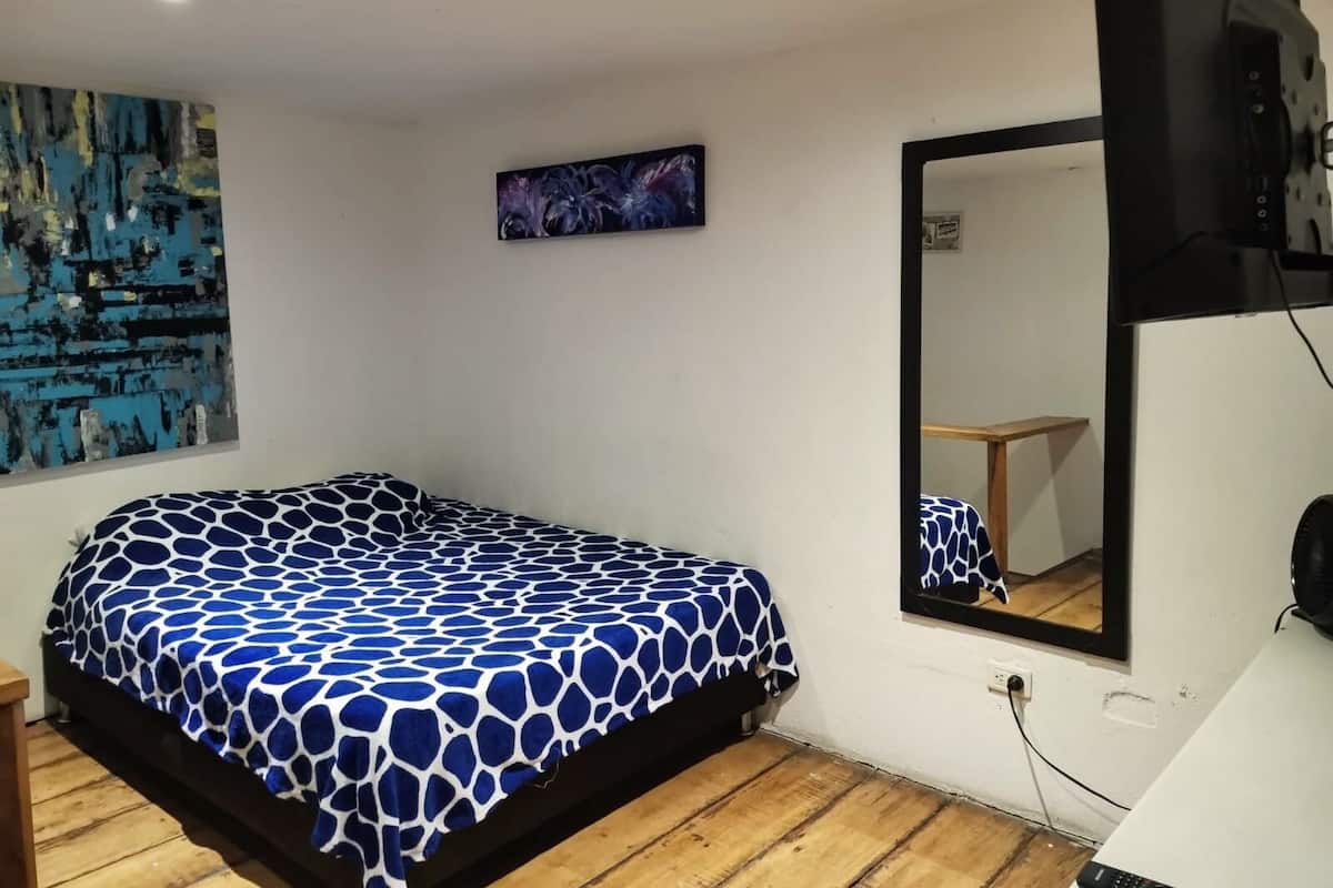 Quarto com uma cama, um quadro abstrato grande, um espelho e piso de madeira.