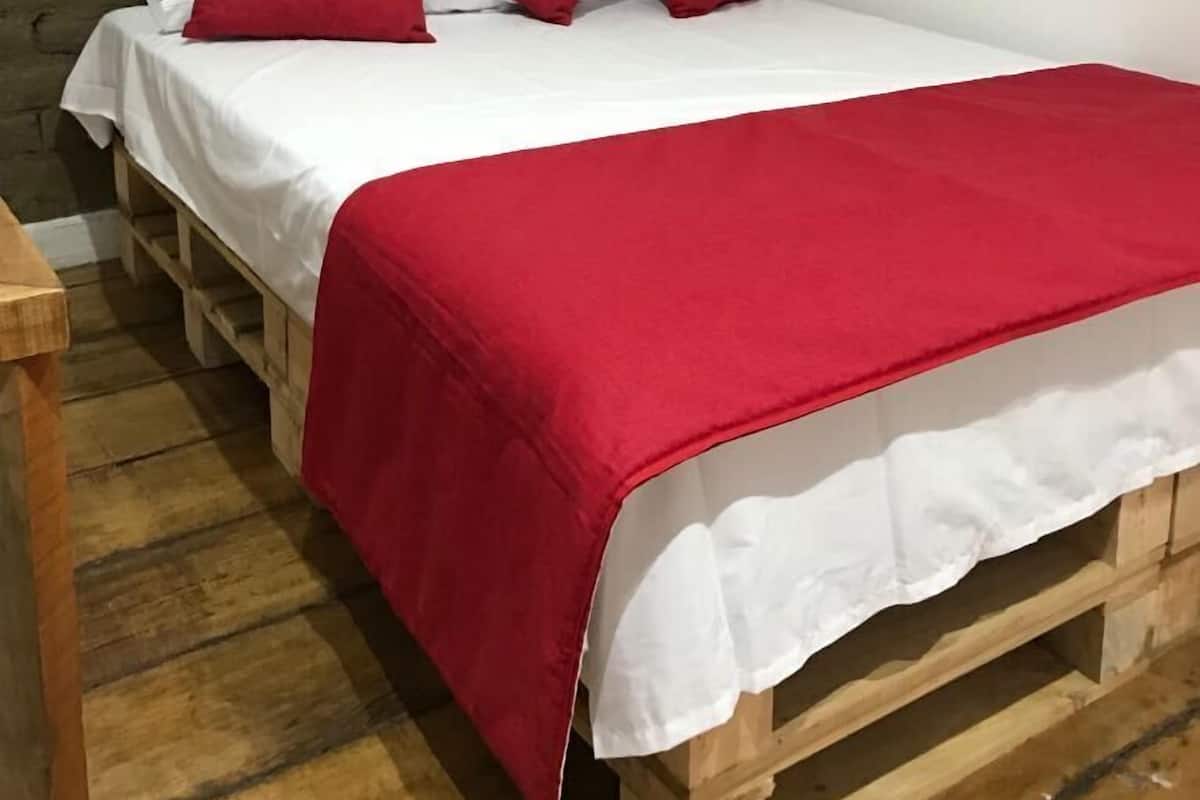Quarto individual com uma cama de solteiro, cabeceira de madeira, roupa de cama branca e almofadas vermelhas.