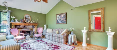 Uma sala de estar com lareira, paredes verdes, um tapete grande e um ventilador de teto.